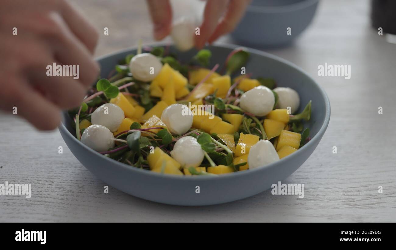 Man put mozzarella balls in salad with micro greens in blue bowl, wide ...