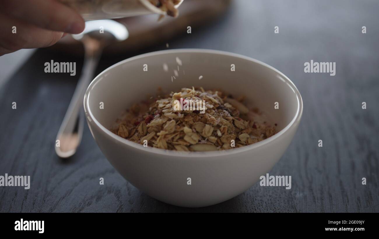 Pour granola over yogurt in white bowl, wide photo Stock Photo - Alamy