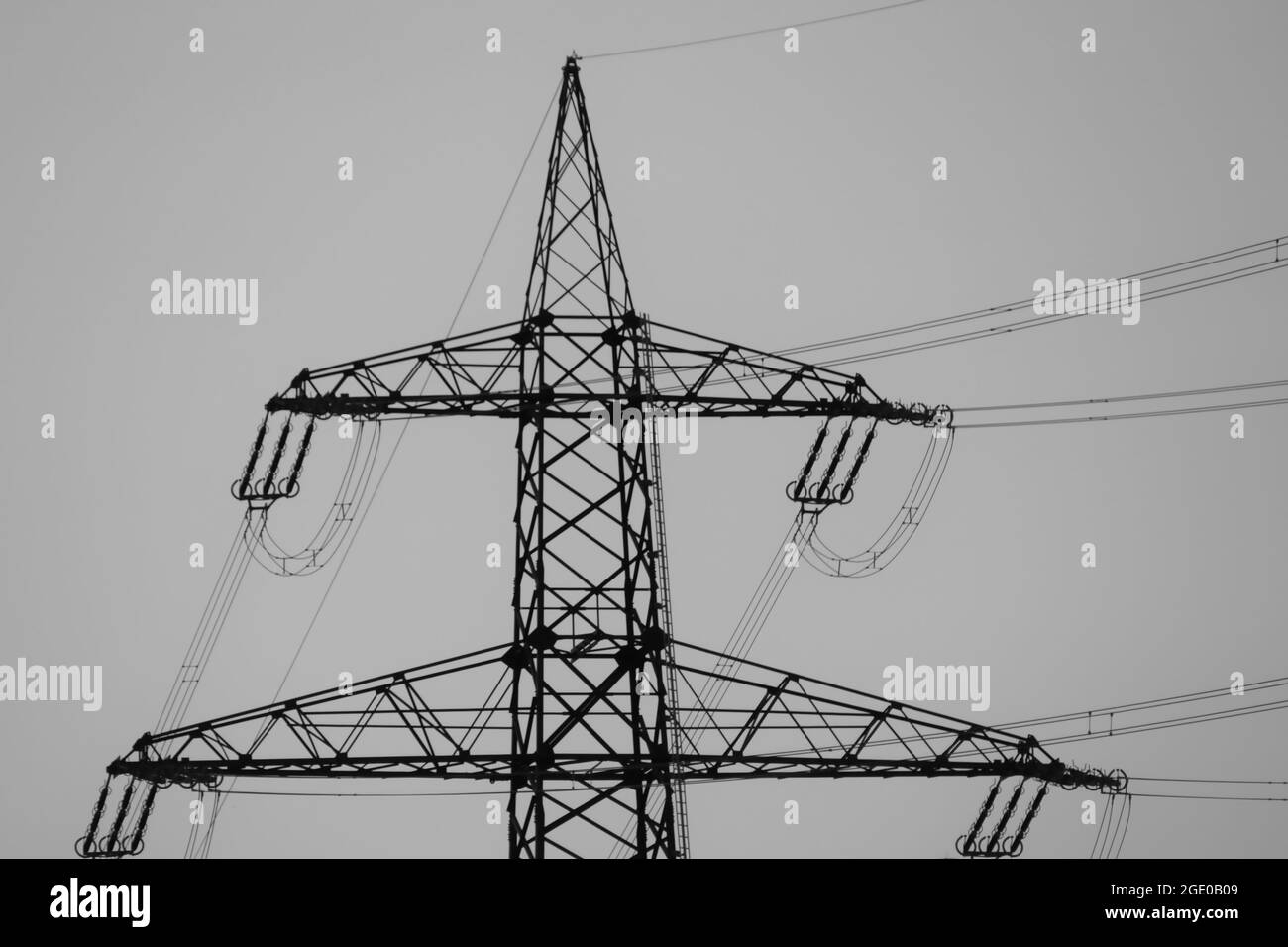 Black silhouette of the upper part of an electricity pylon against a ...