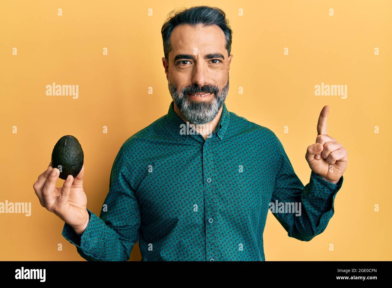 Middle age man with beard and grey hair holding avocado smiling with an ...
