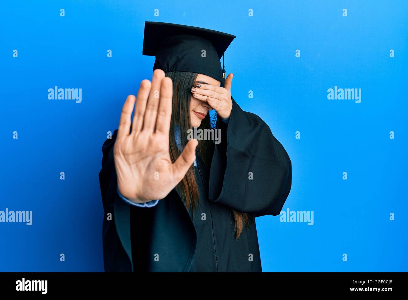 Beautiful brunette young woman wearing graduation cap and ceremony robe ...