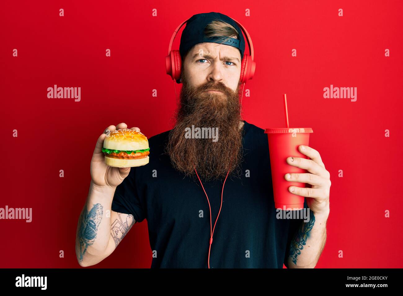 Redhead man with long beard eating a tasty classic burger and drinking ...