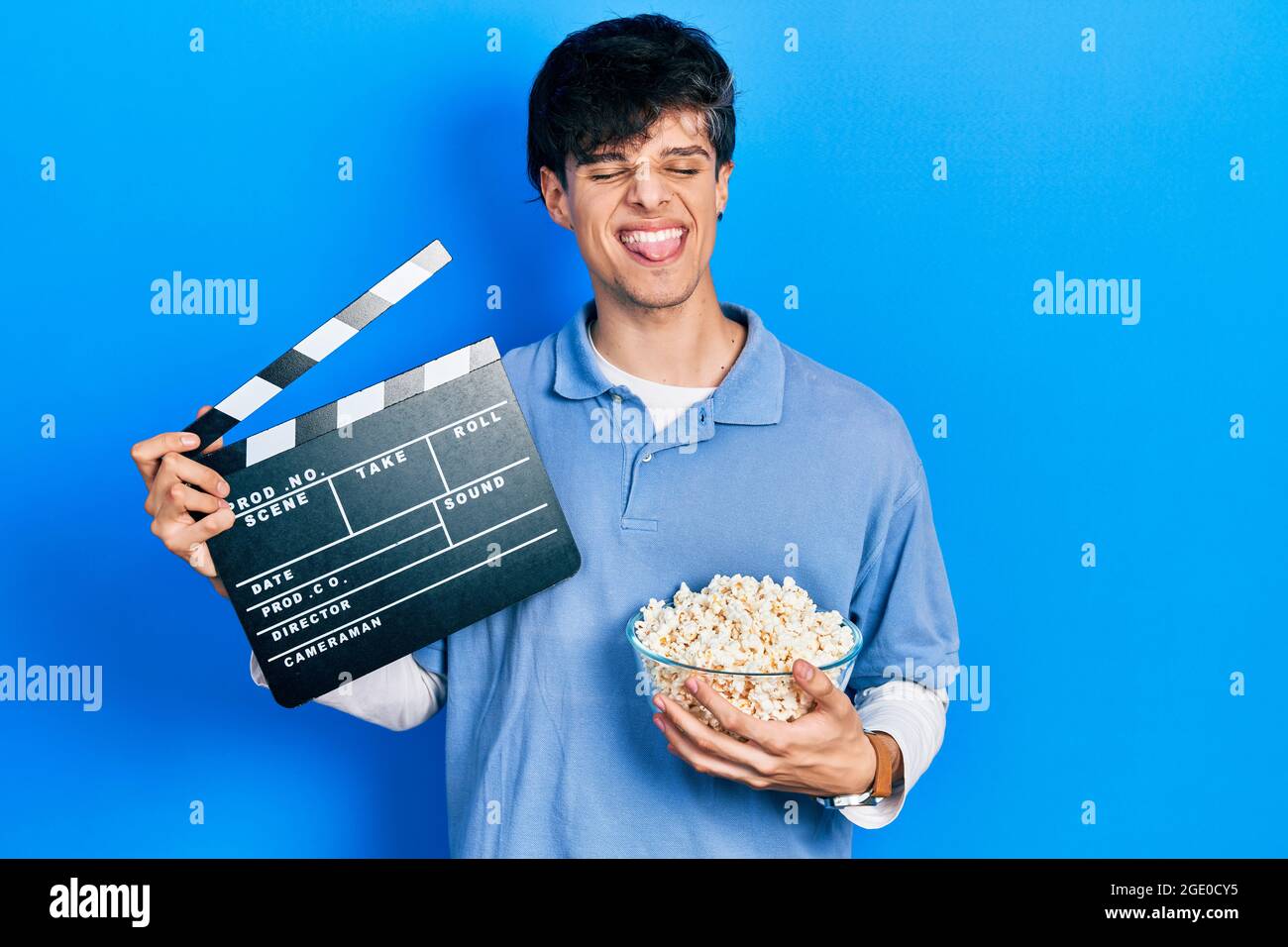 Handsome hipster young man eating popcorn holding cinema clapboard ...