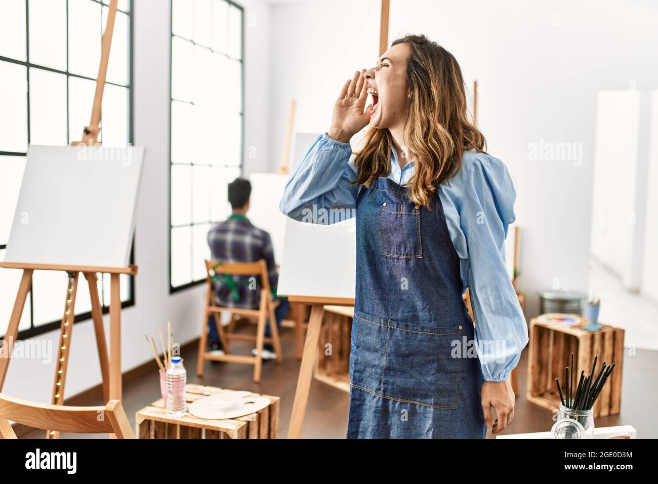 Young artist woman at art studio shouting and screaming loud to side ...