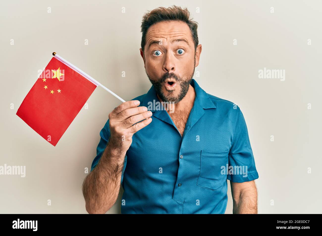 Middle age man holding china flag scared and amazed with open mouth for ...
