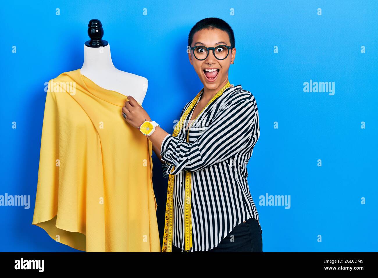 Beautiful hispanic woman with short hair standing by manikin sewing ...