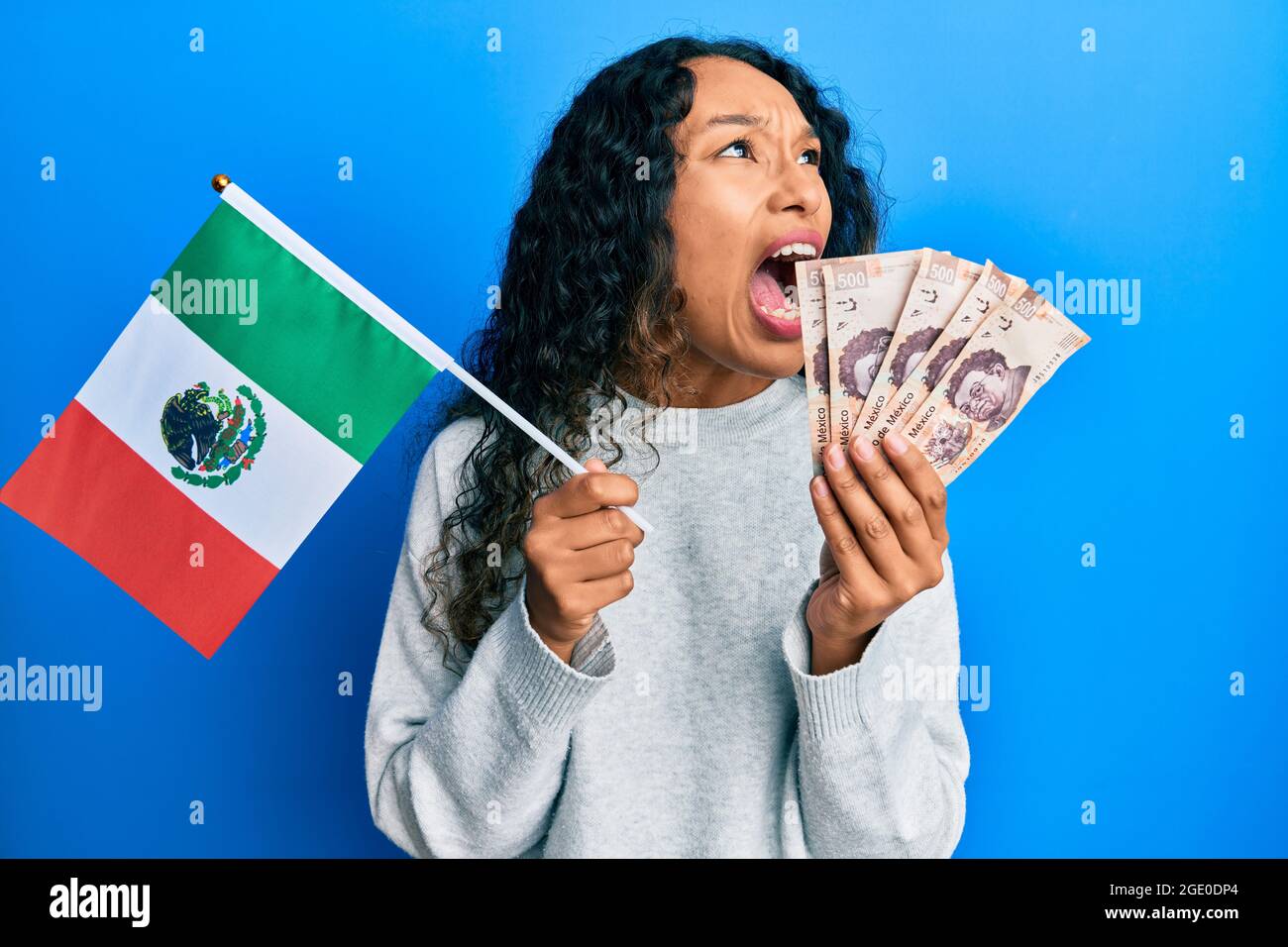 Young latin woman holding mexico flag and mexican pesos banknotes angry ...