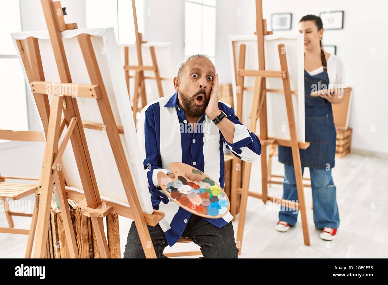 Senior artist man at art studio afraid and shocked, surprise and amazed ...