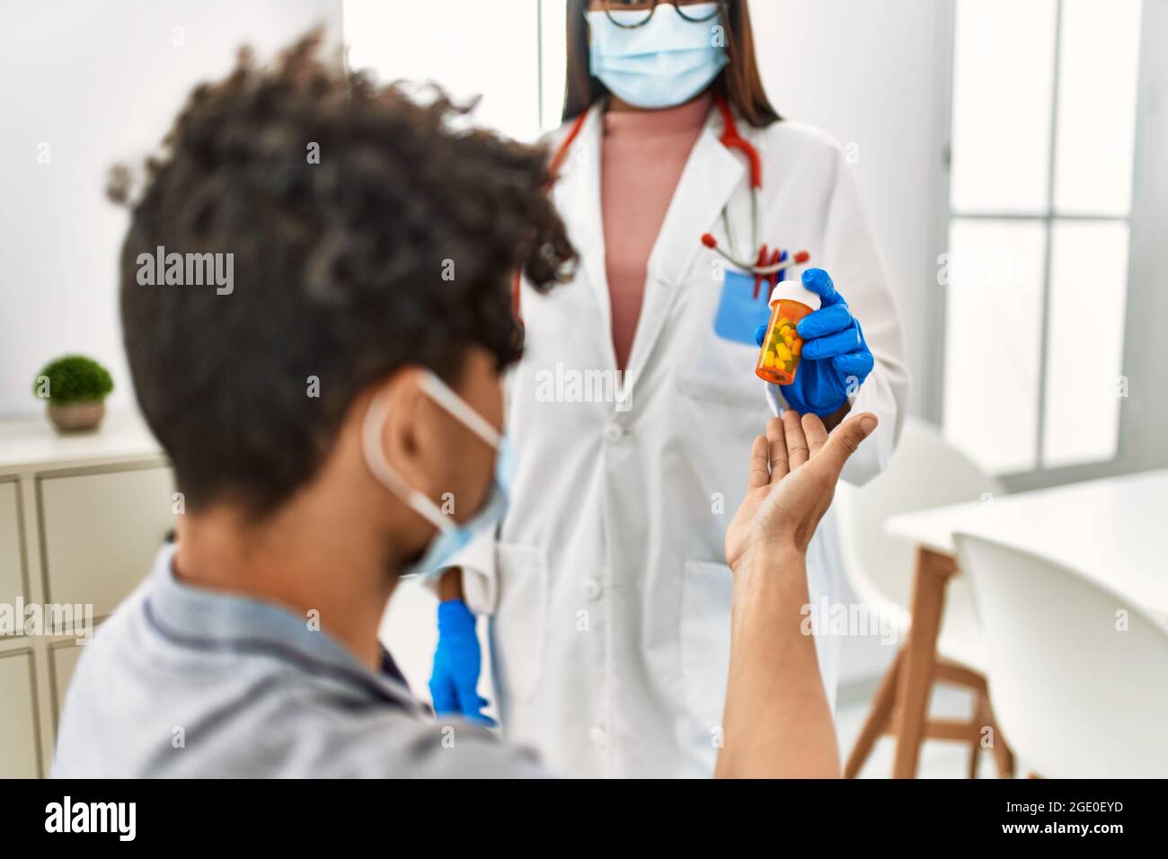 Young latin doctor woman giving bottle of pills to man at medical room ...
