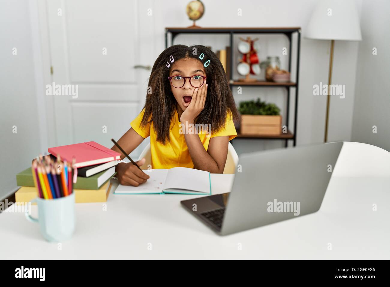 Young african american girl doing homework at home afraid and shocked ...