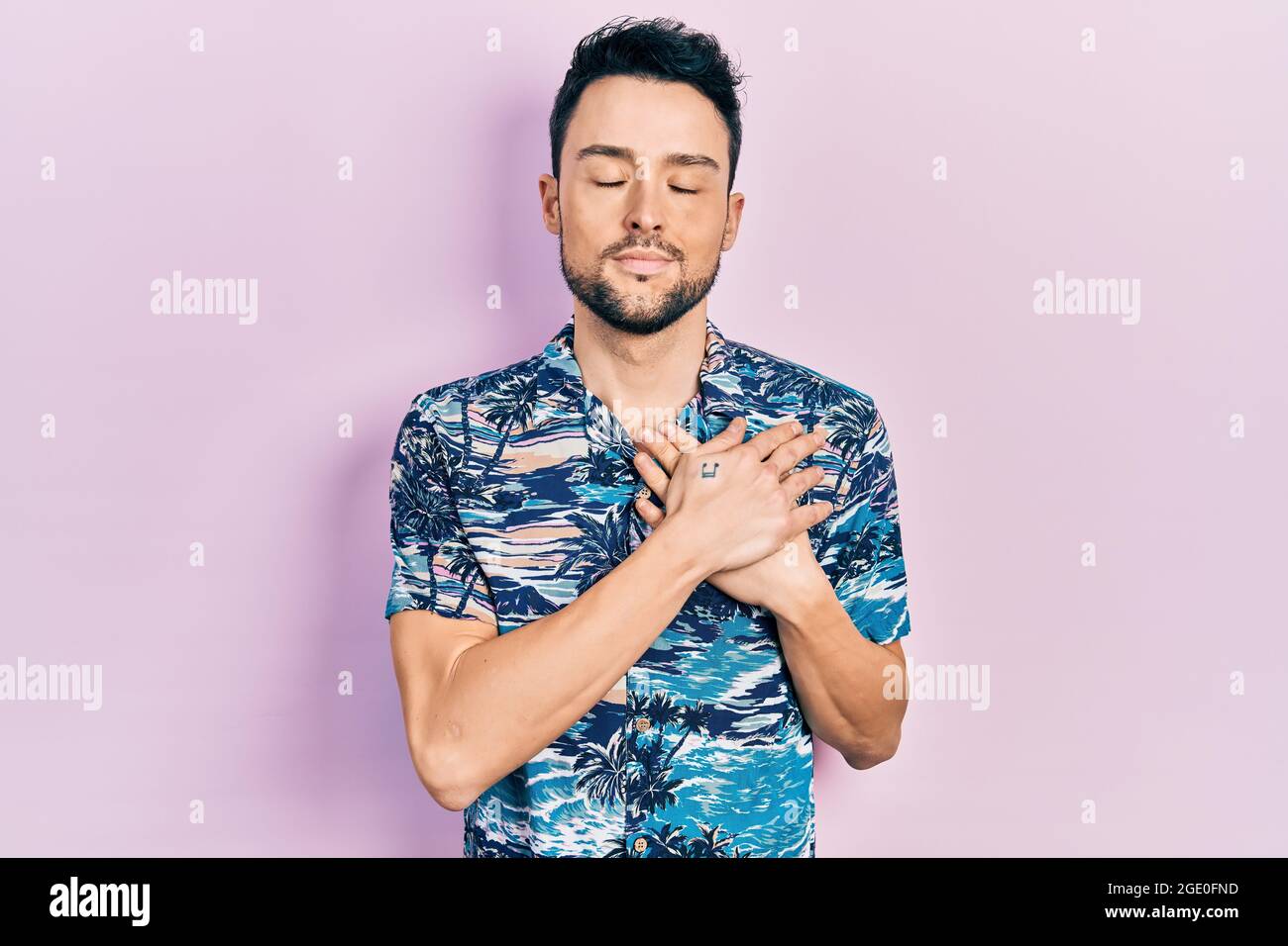 Young hispanic man wearing casual clothes smiling with hands on chest with closed eyes and ...