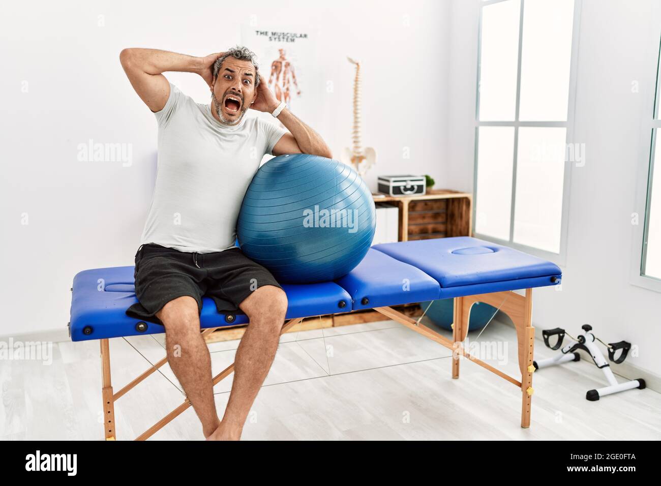 Middle age hispanic man at pain recovery clinic holding pilates ball ...