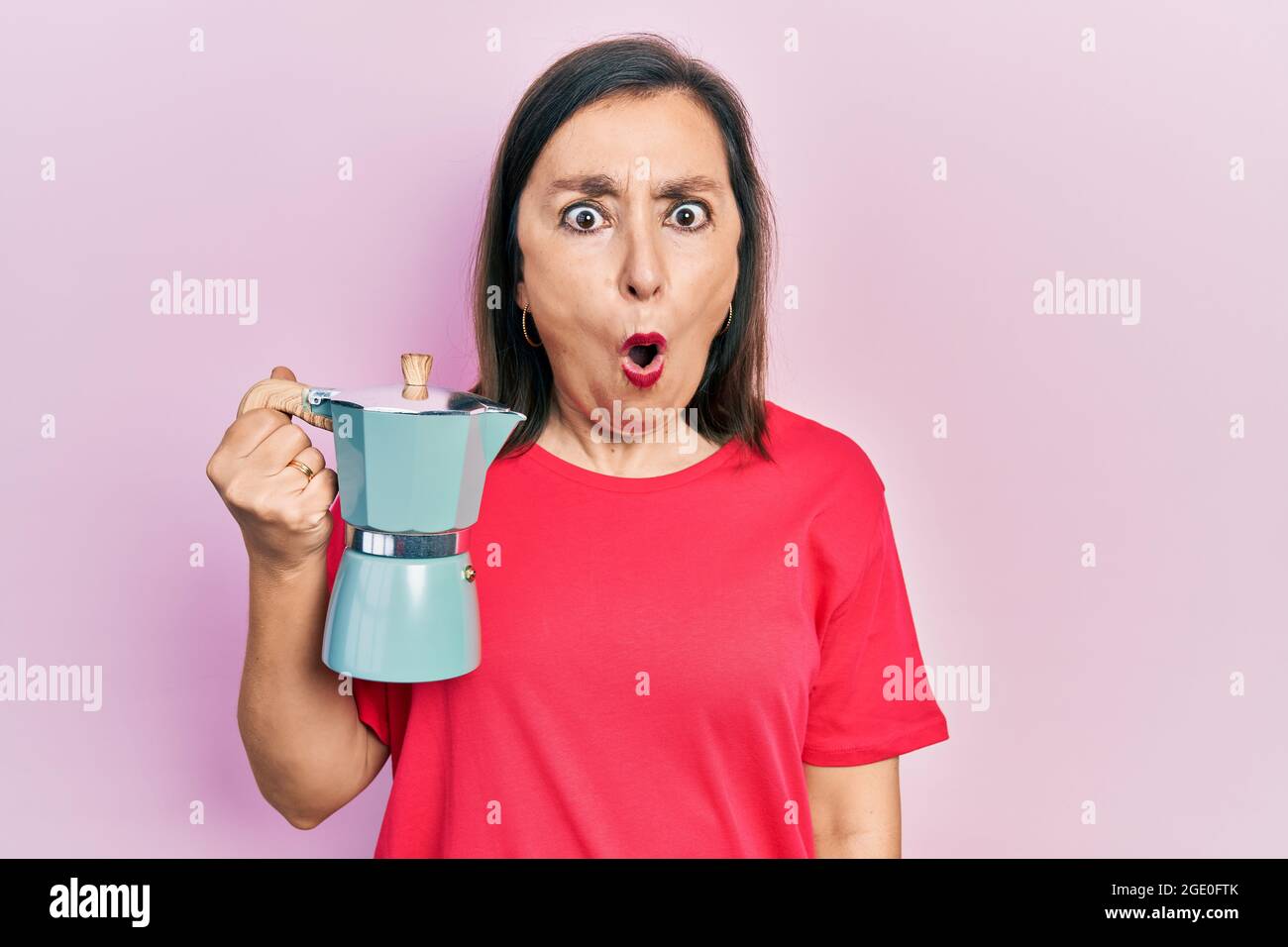 Middle age hispanic woman holding italian coffee maker scared and ...