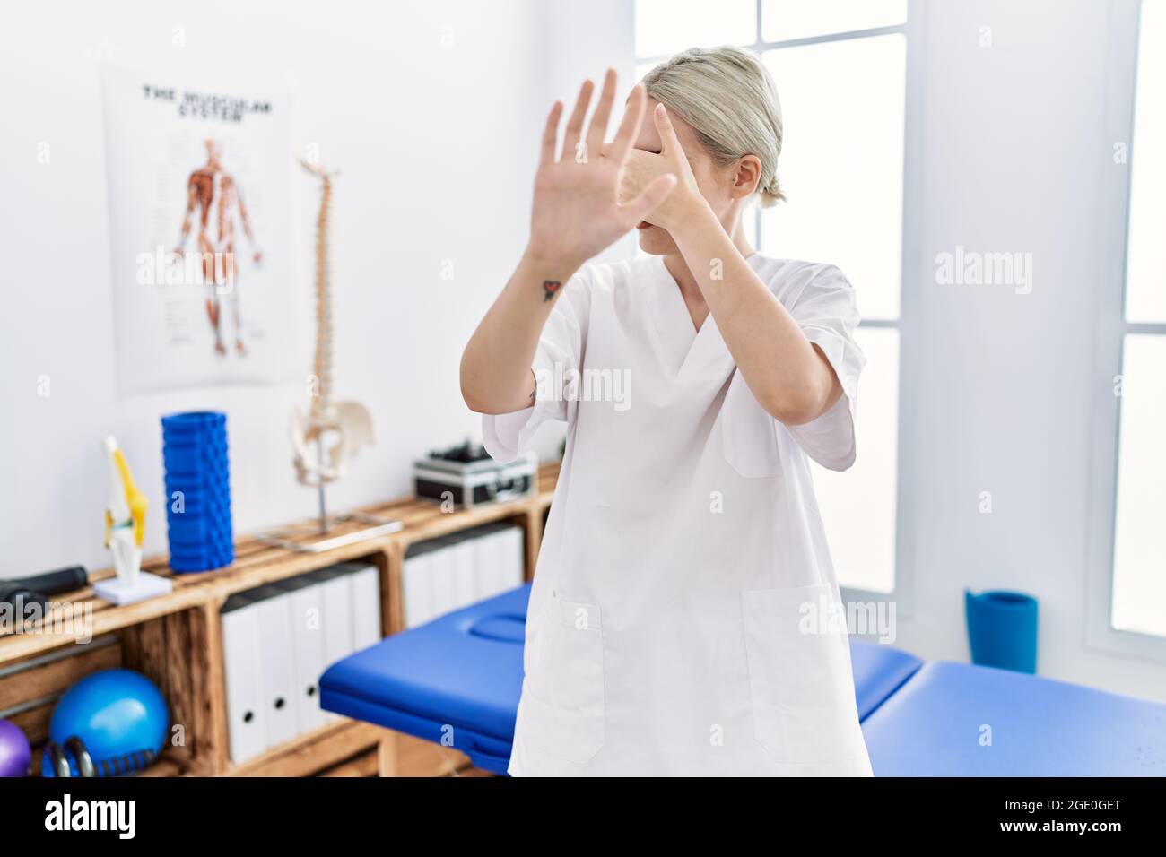Young caucasian woman working at pain recovery clinic covering eyes ...
