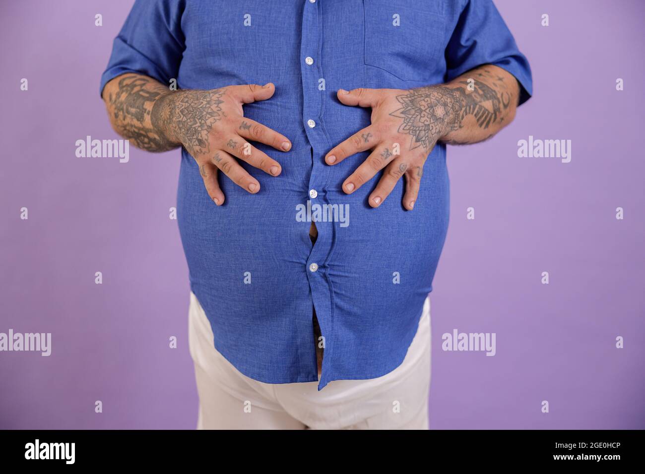 Man with overweight and tattoos holds hands on large belly on purple ...
