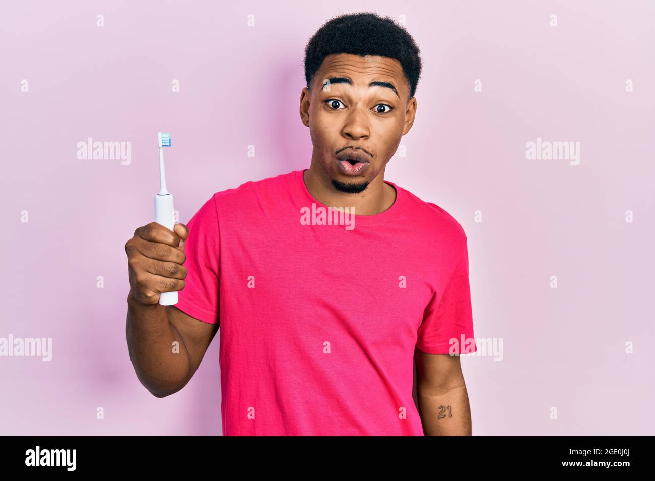 Young african american man holding electric toothbrush scared and ...