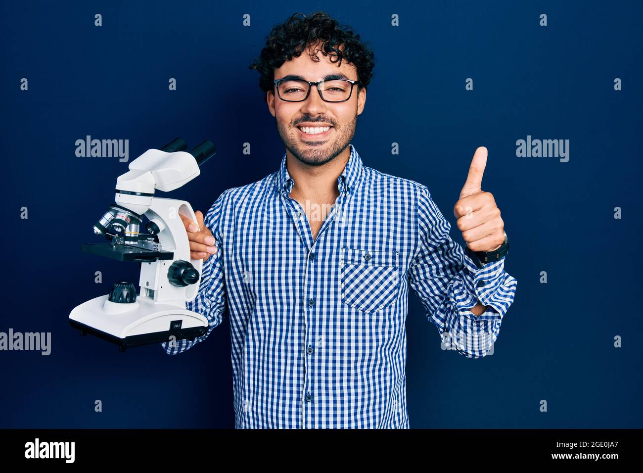 Young hispanic man holding microscope smiling happy and positive, thumb ...