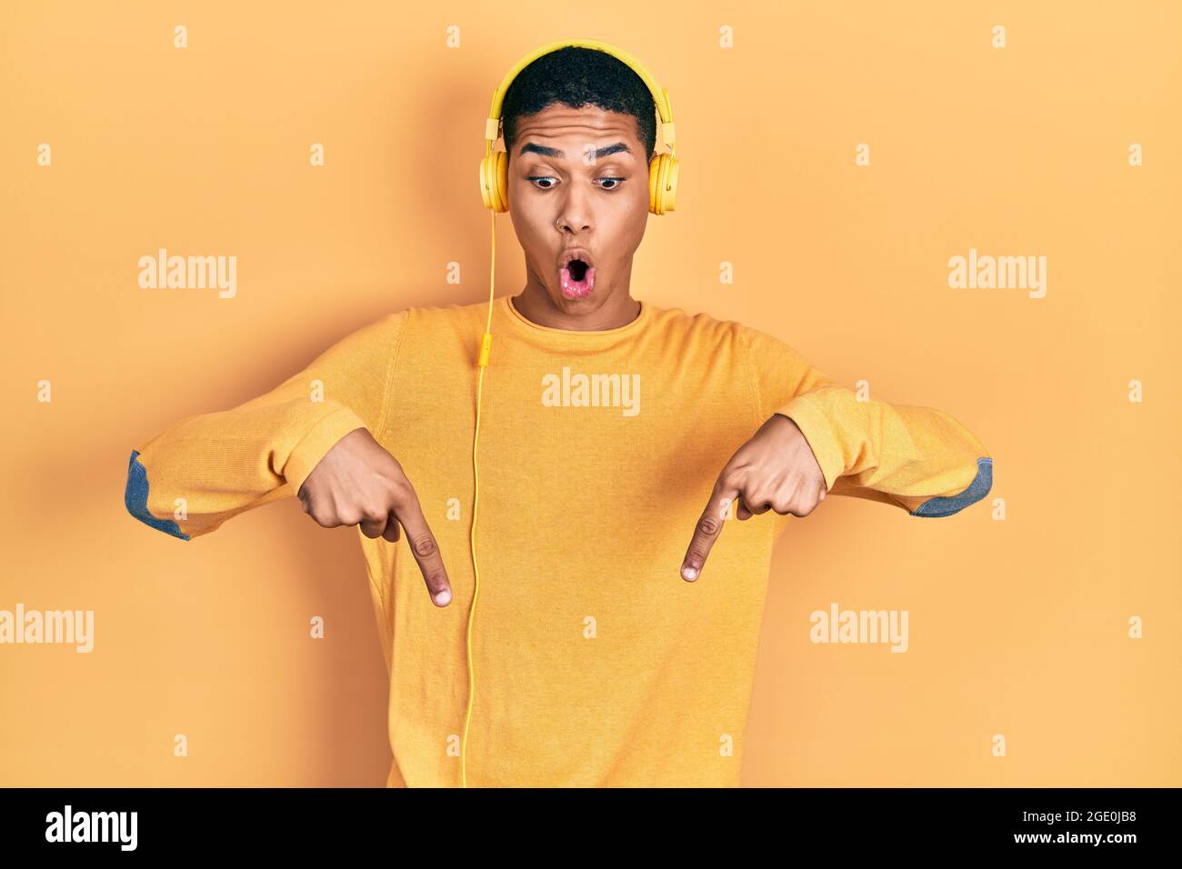 Young african american guy listening to music using headphones pointing ...