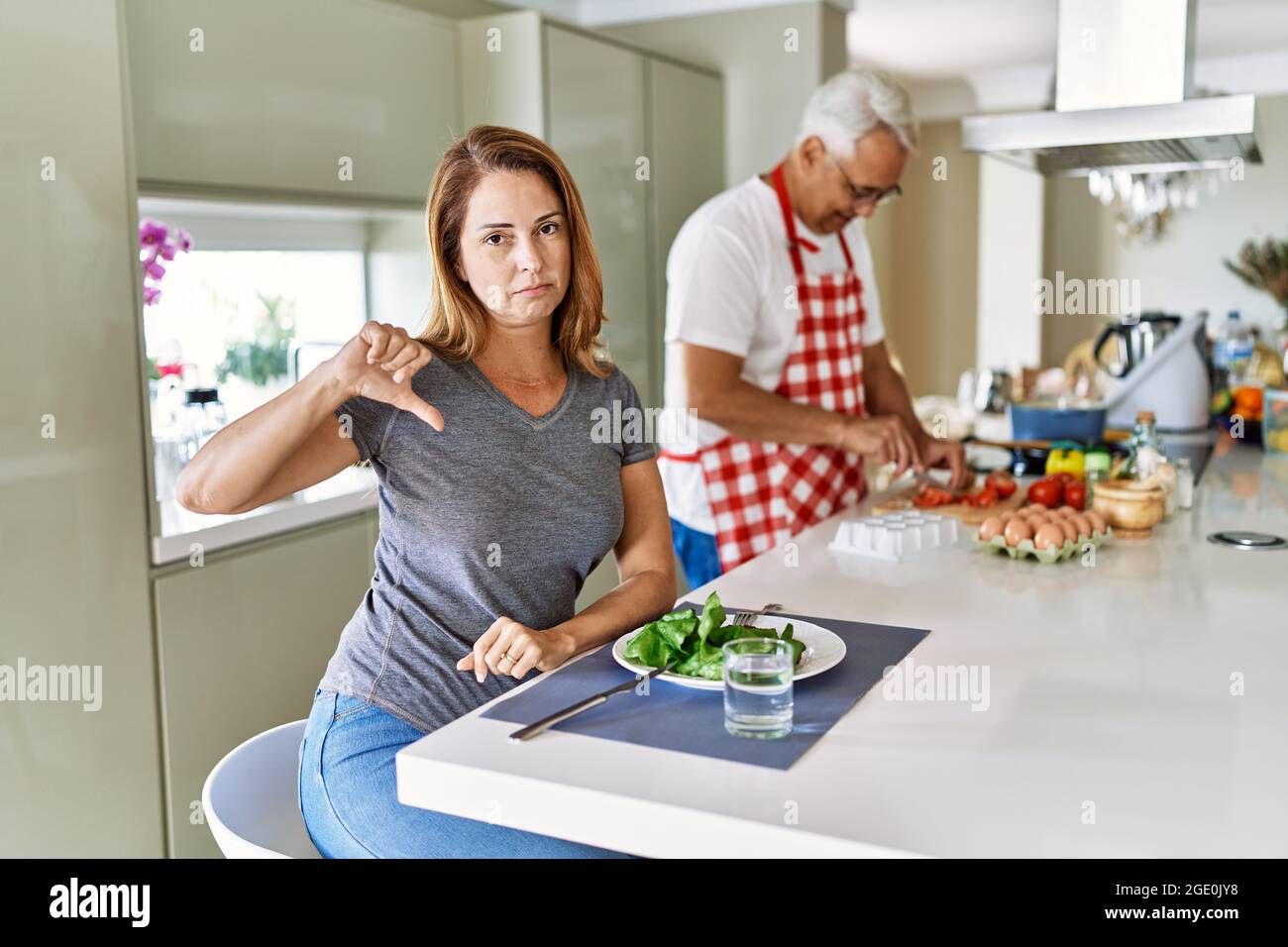 Middle age hispanic couple eating healthy salad at home with angry face ...