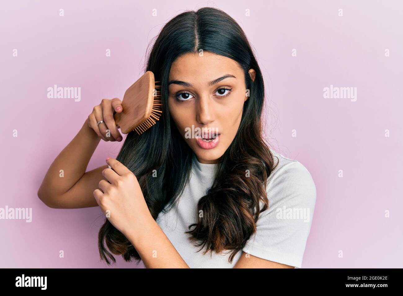 Young hispanic woman styling hair using comb in shock face, looking ...