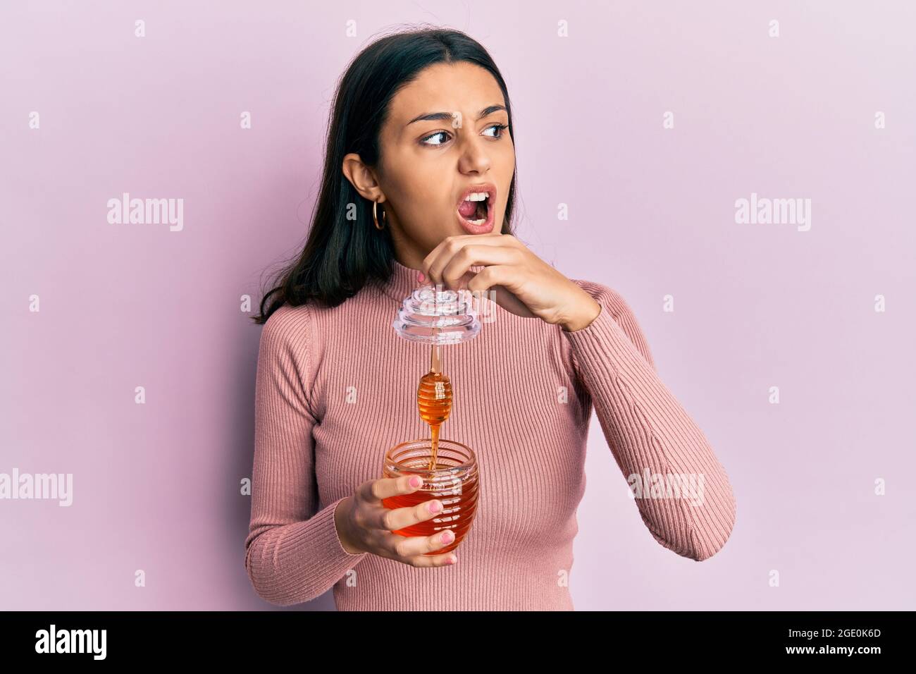 Young hispanic woman holding honey angry and mad screaming frustrated ...