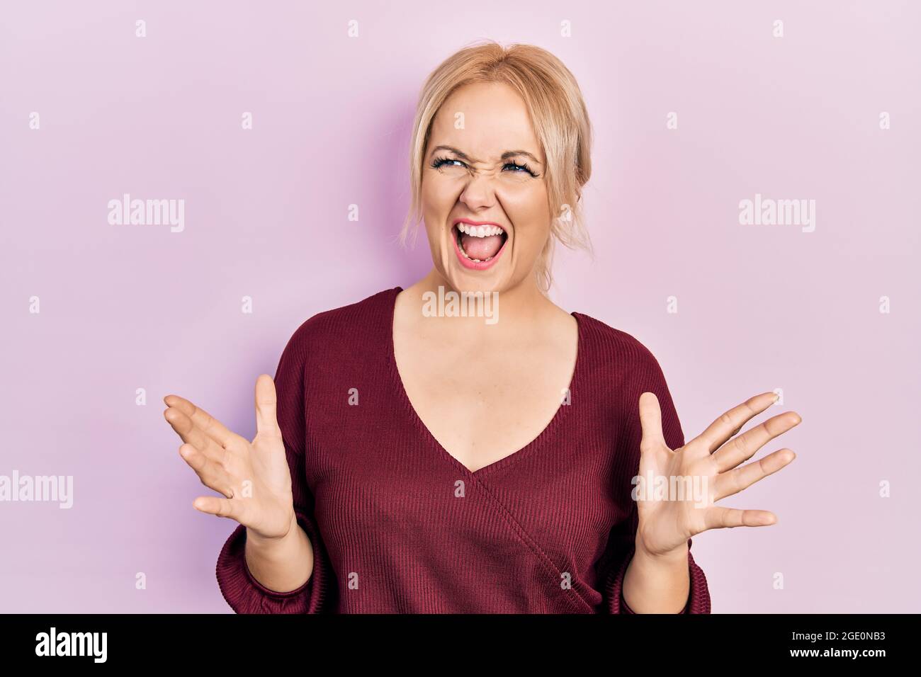 Young blonde woman wearing casual winter sweater crazy and mad shouting ...