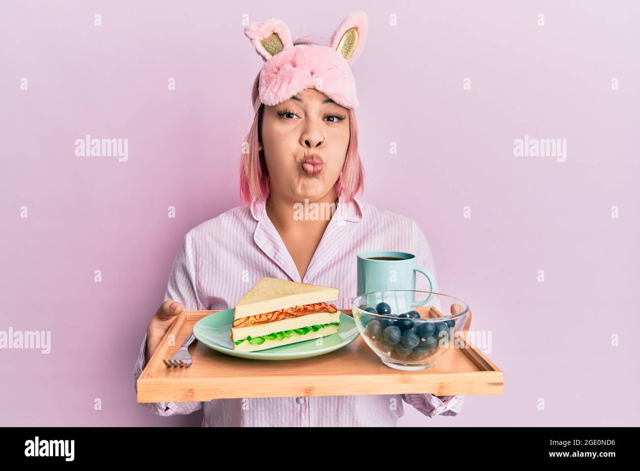 Hispanic woman with pink hair wearing pajama holding healthy breakfast ...