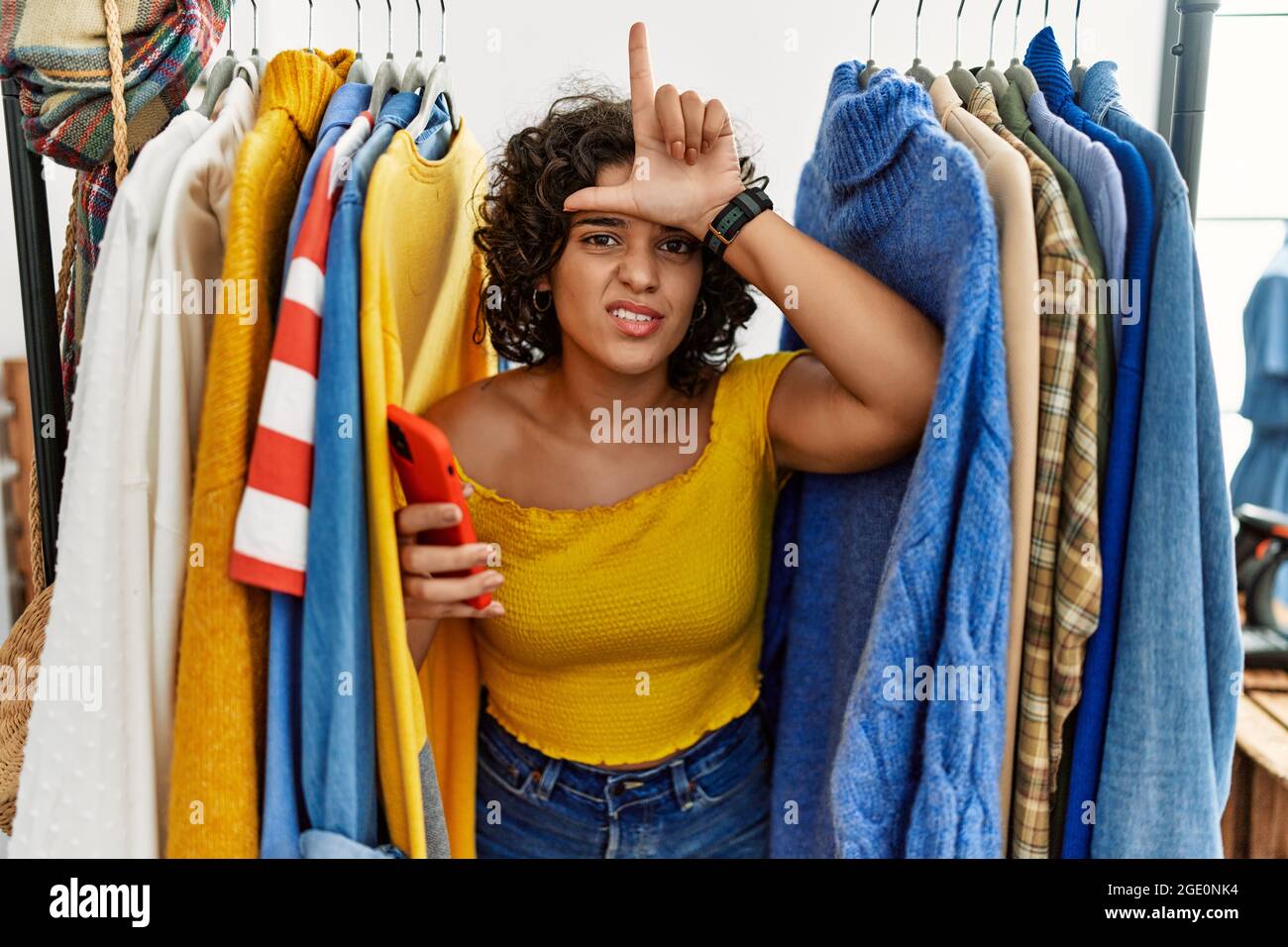 Young hispanic woman searching clothes on clothing rack using ...