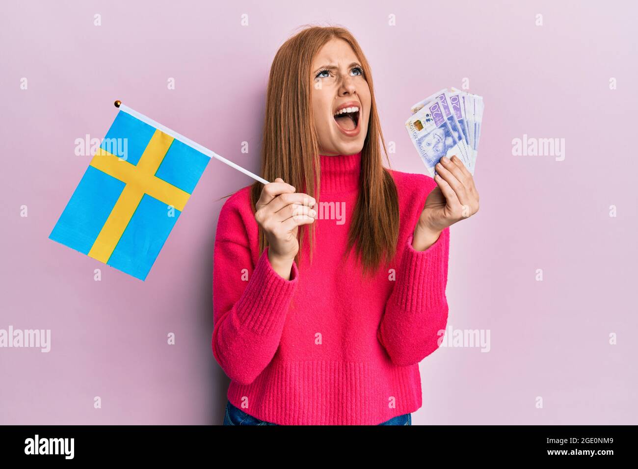 Young irish woman holding sweden flag and krone banknotes angry and mad ...