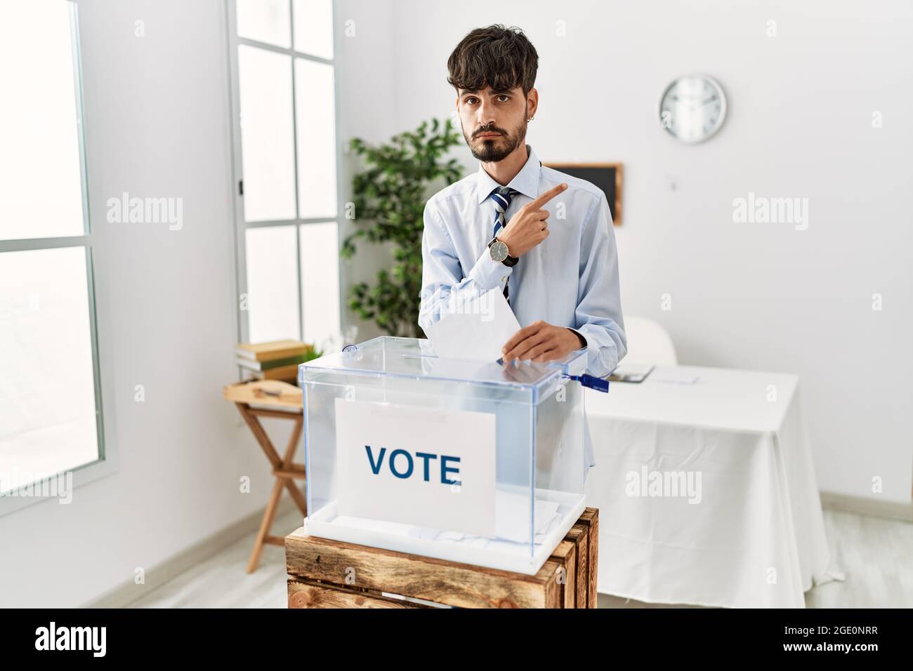 Hispanic man with beard voting putting envelop in ballot box pointing ...