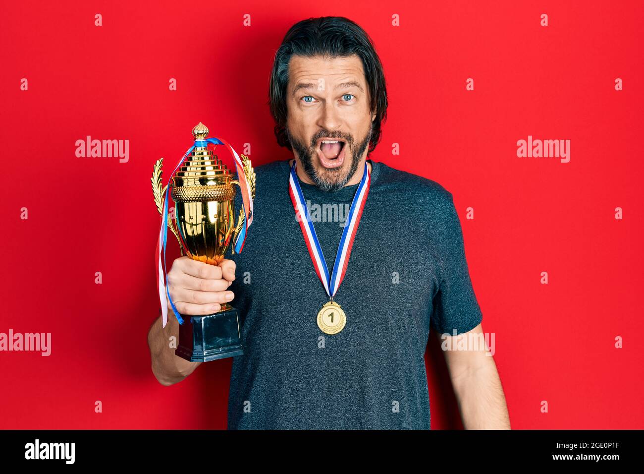 Middle age caucasian man holding champion trophy wearing medals scared ...