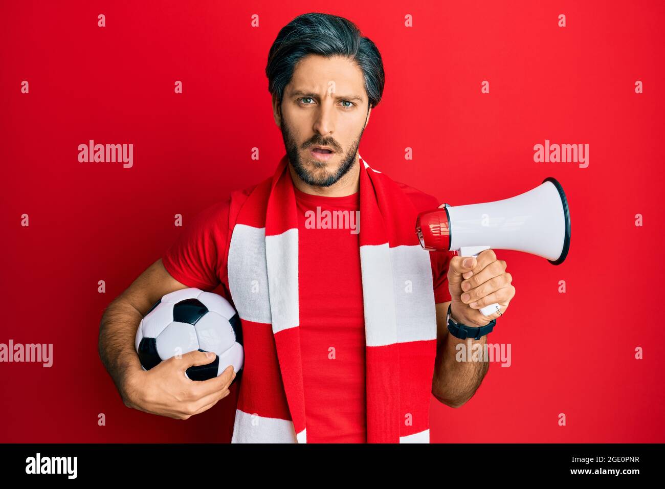 Young hispanic man football hooligan holding ball using megaphone in ...