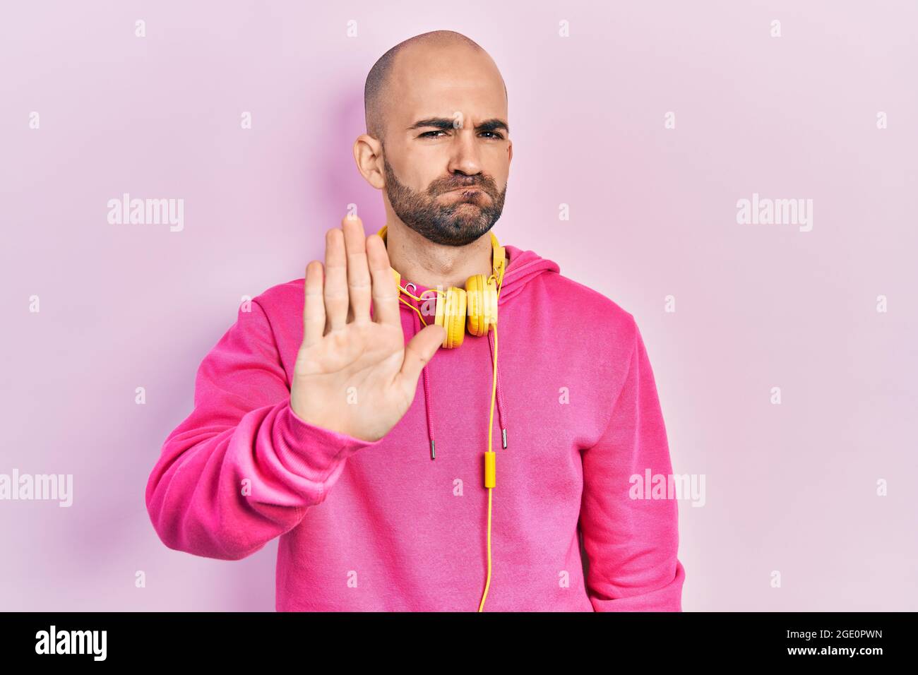 Young bald man wearing gym clothes and using headphones doing stop sing ...