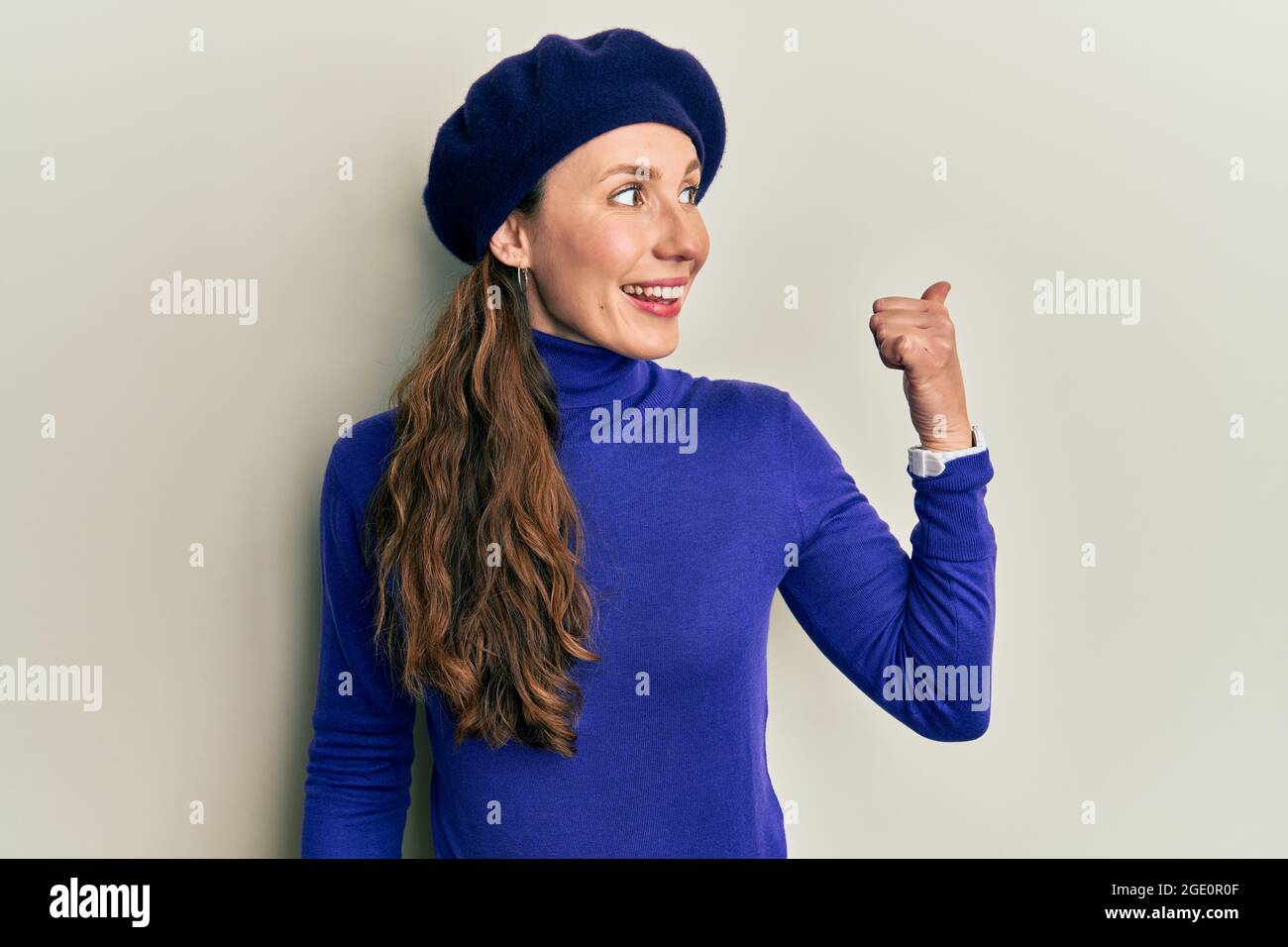 Young blonde woman wearing french look with beret pointing thumb up to ...