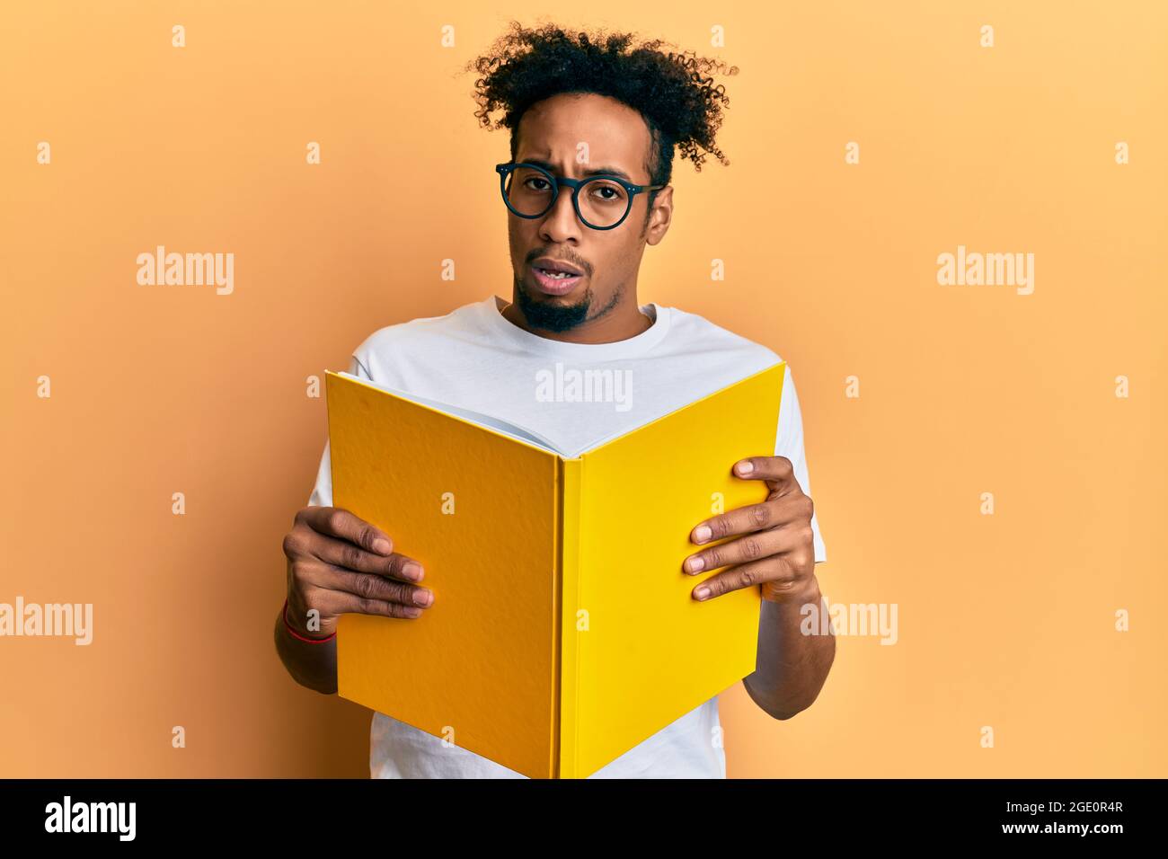 Young african american man with beard reading a book wearing glasses in ...