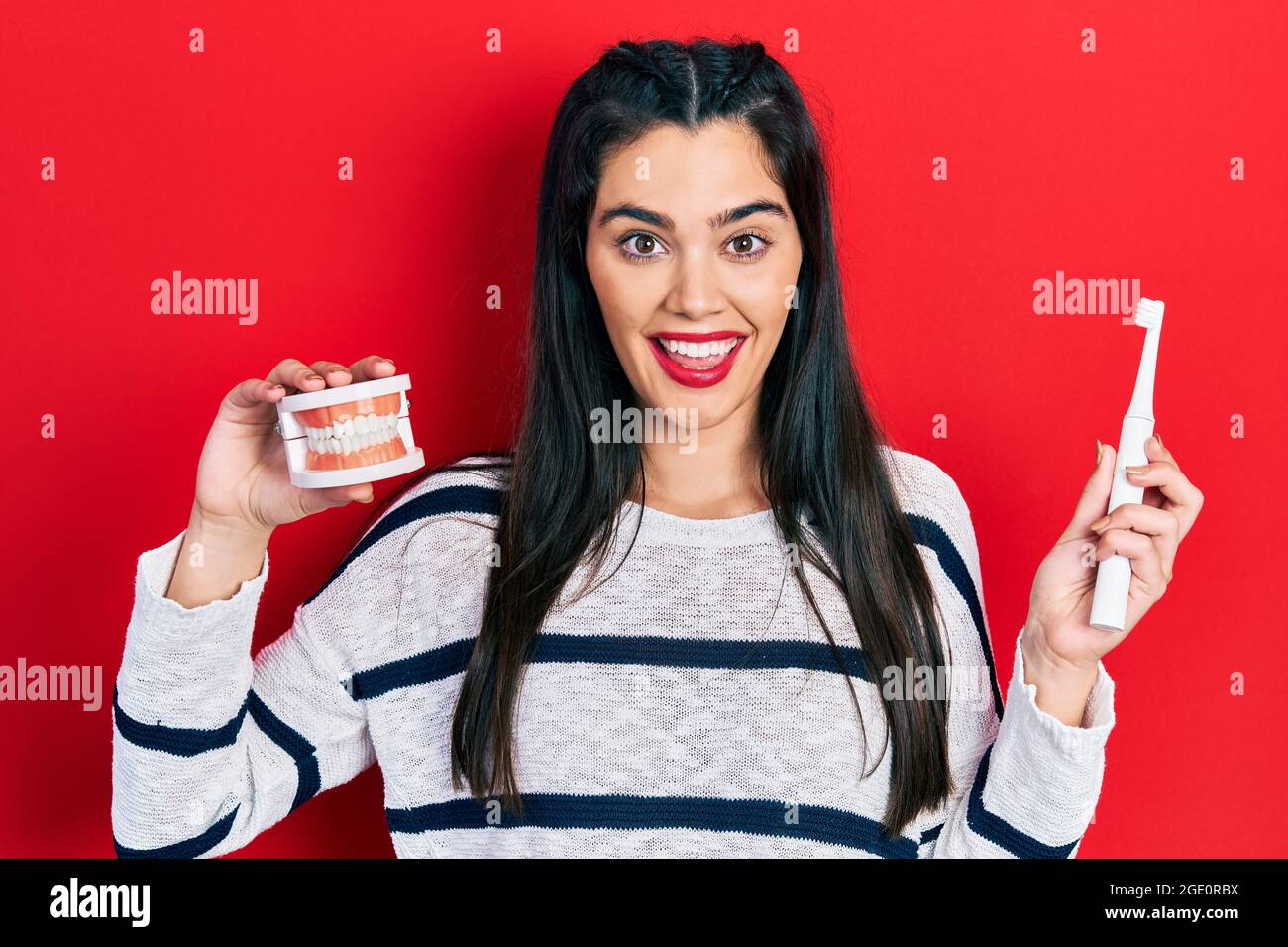 Young hispanic girl holding electric toothbrush and denture celebrating ...