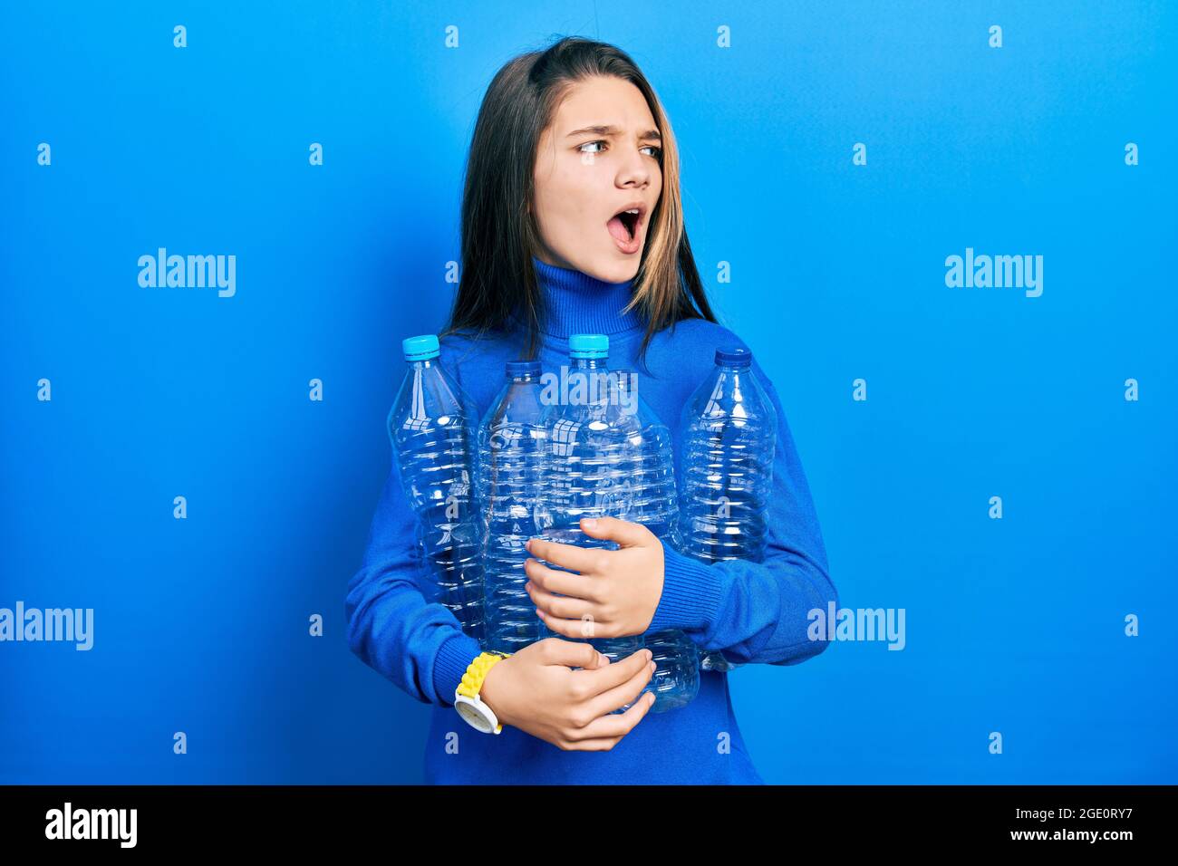 Young brunette girl holding recycling plastic bottles angry and mad ...