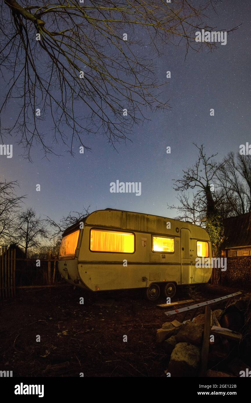 Old white caravan trailer with yellow illumination in backyard at stary ...