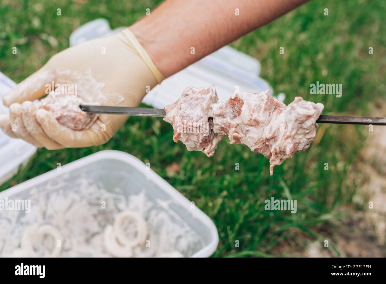 Male hands in white gloves stringing raw meat in marinade on skewers ...