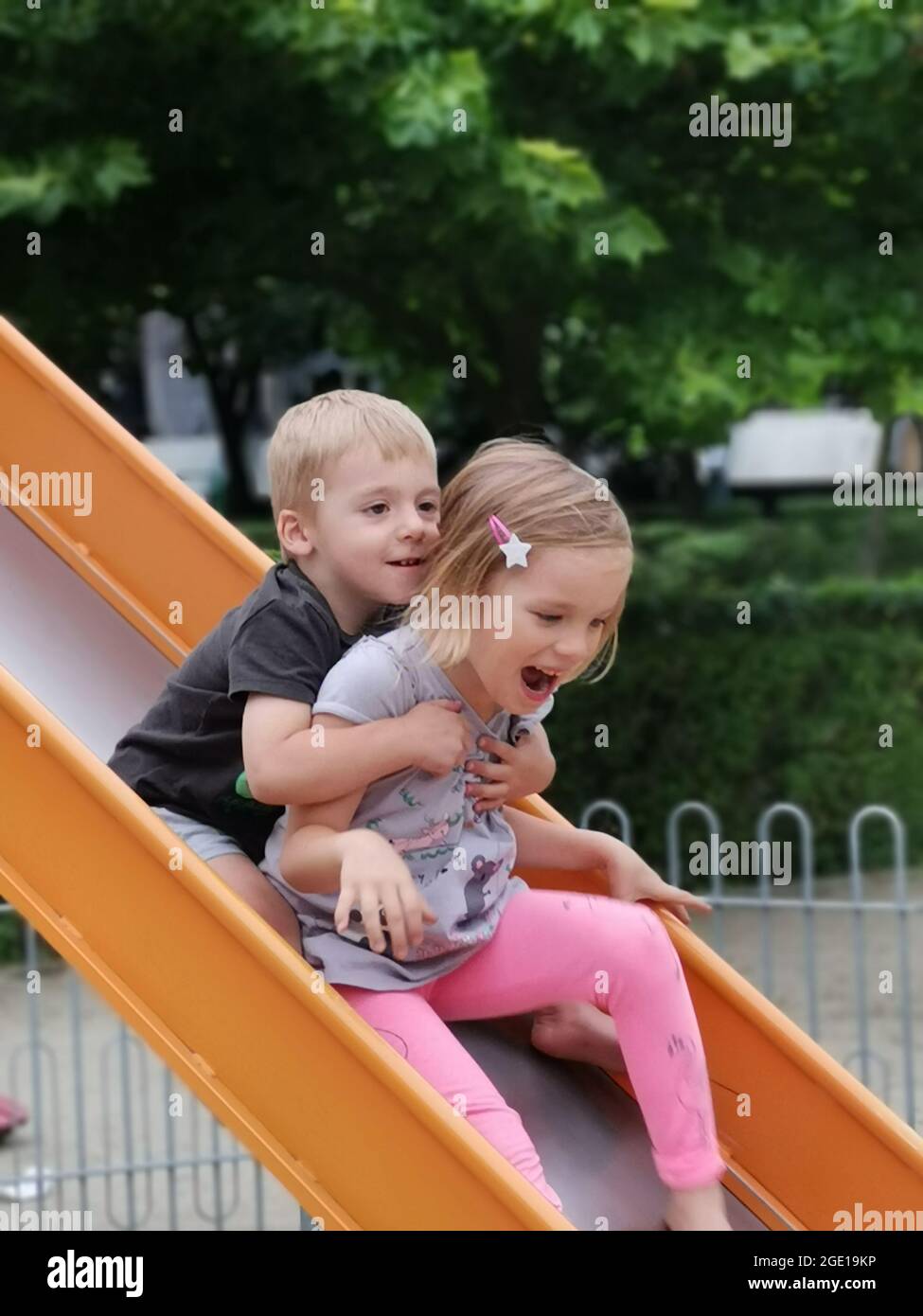 A cute Caucasian little girl and boy sliding on a slide in the ...