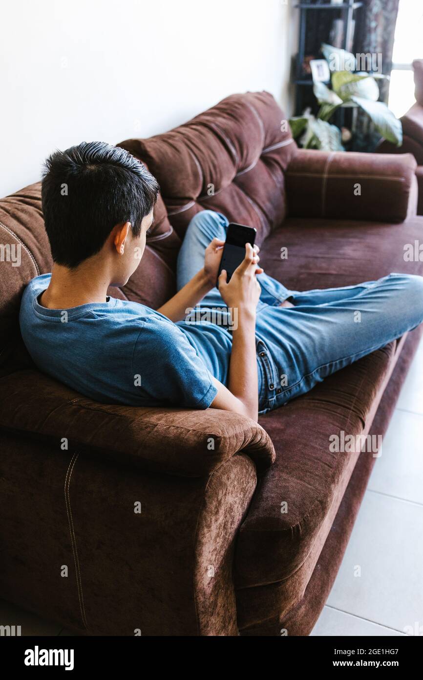 Young mexican teenager using smart phone sitting on sofa at home in ...