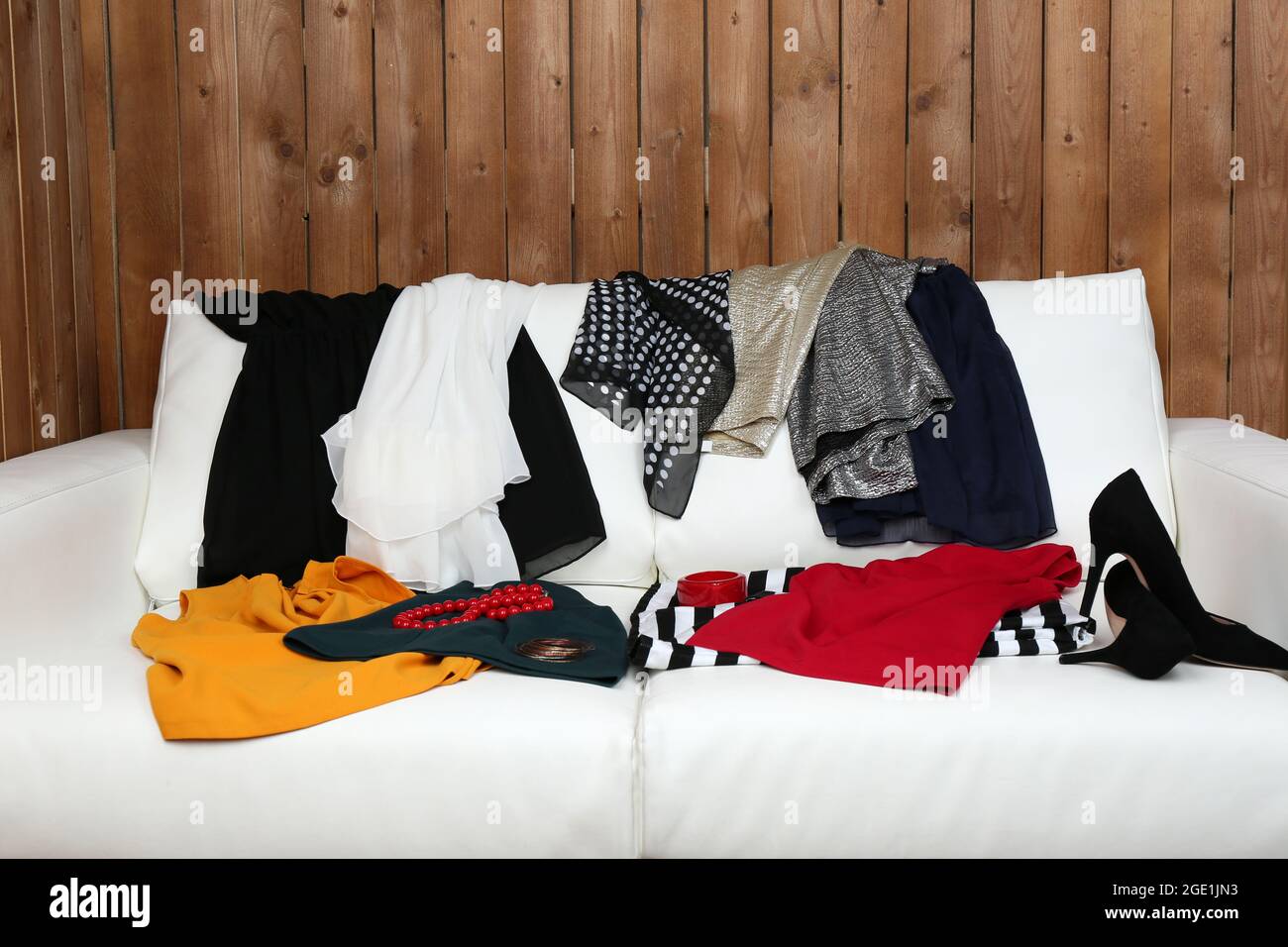 Messy clothing with shoes on white sofa, on wooden planks background ...