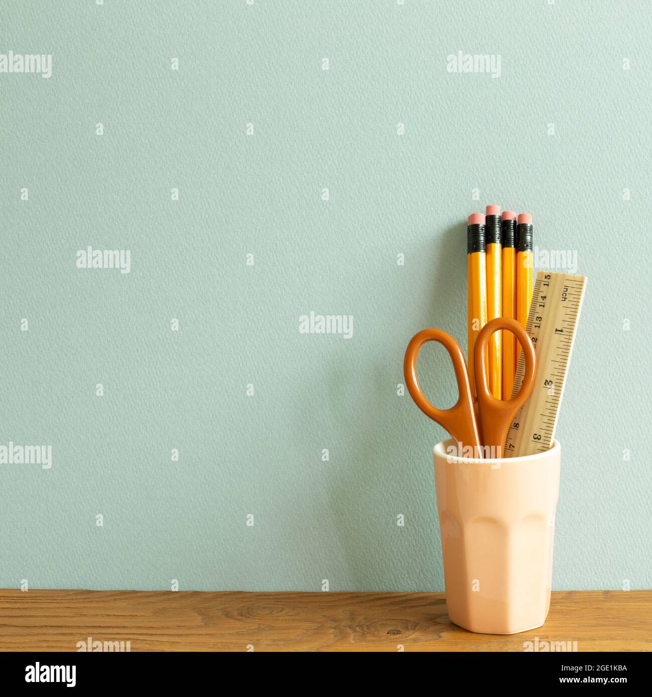 Pencils, ruler and scissors in holder on wooden desk. blue wall ...