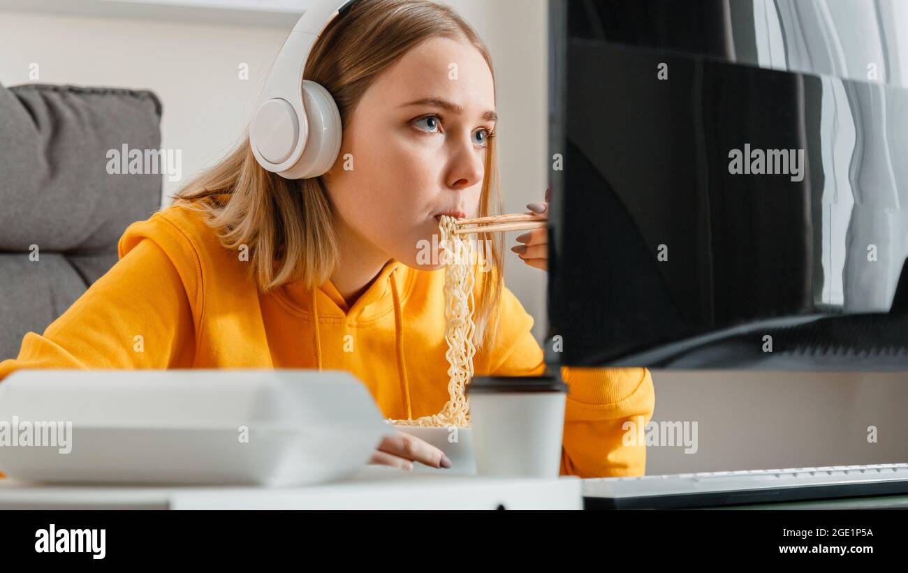 Hungry female gamer eats noodles Chinese dish at home interior using ...