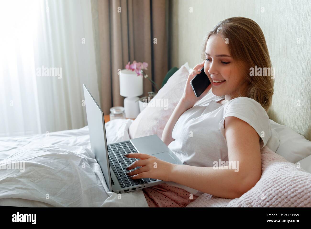 Smiling young woman in pajamas lying in bed working use laptop ...