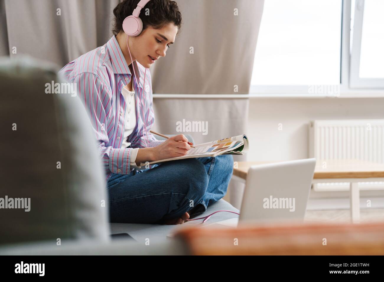 A woman in headphones writing something while sitting with her legs on ...