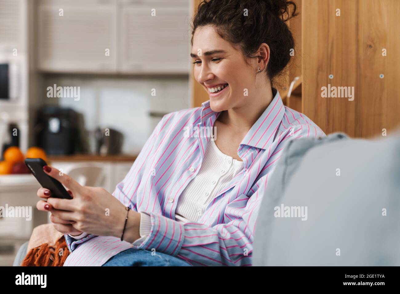 The smiling woman looking at the phone while sitting on the couch in ...