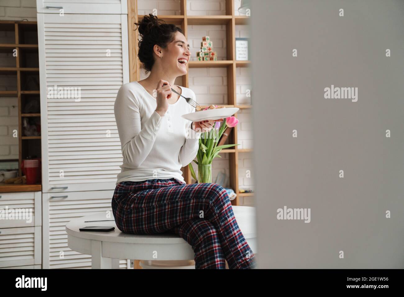 The laughing woman sticking food on fork while sitting at kitchen table ...