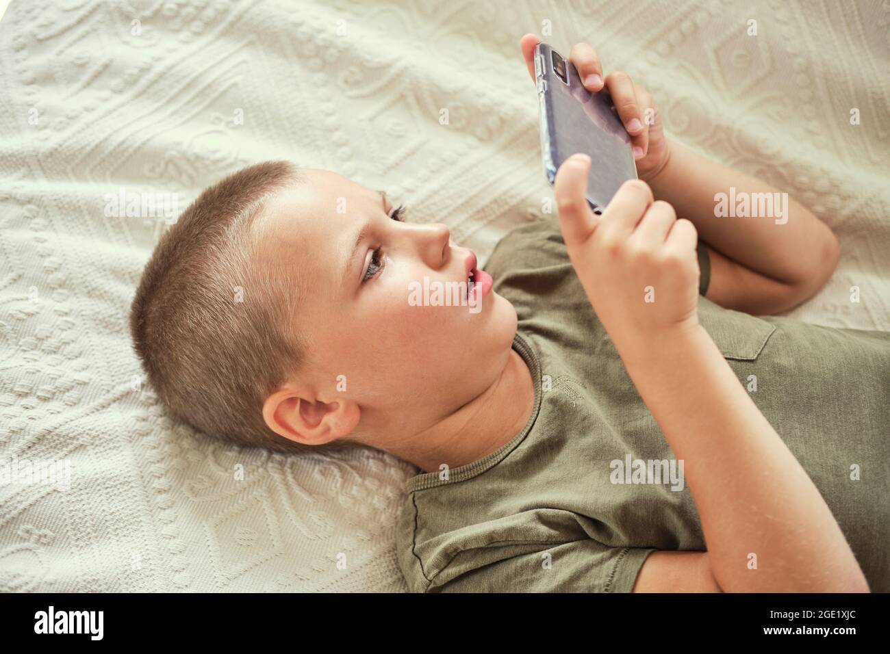 Young boy lying on the bed and playing smartphone. Internet ...