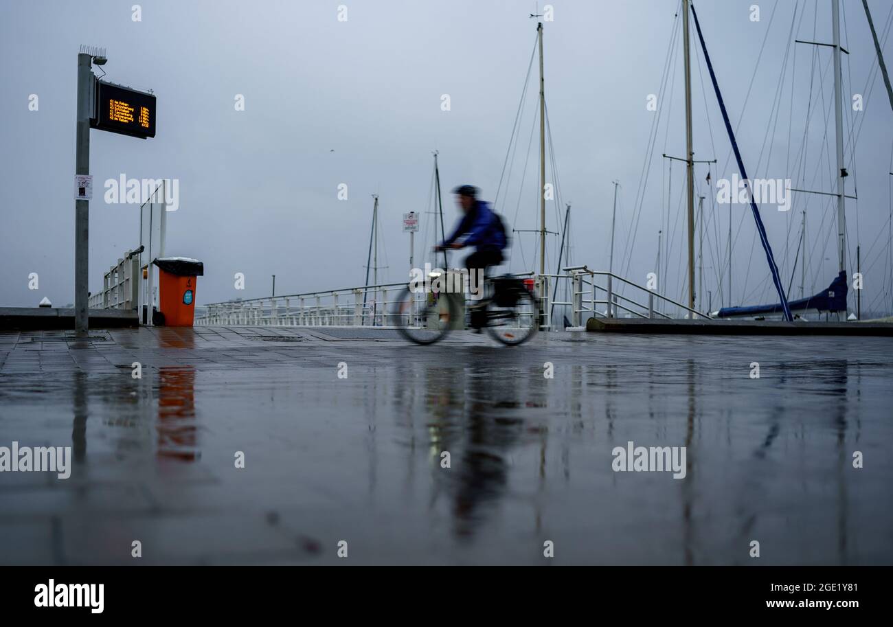 Kiel, Germany. 16th Aug, 2021. A cyclist passes a jetty on the shore of ...